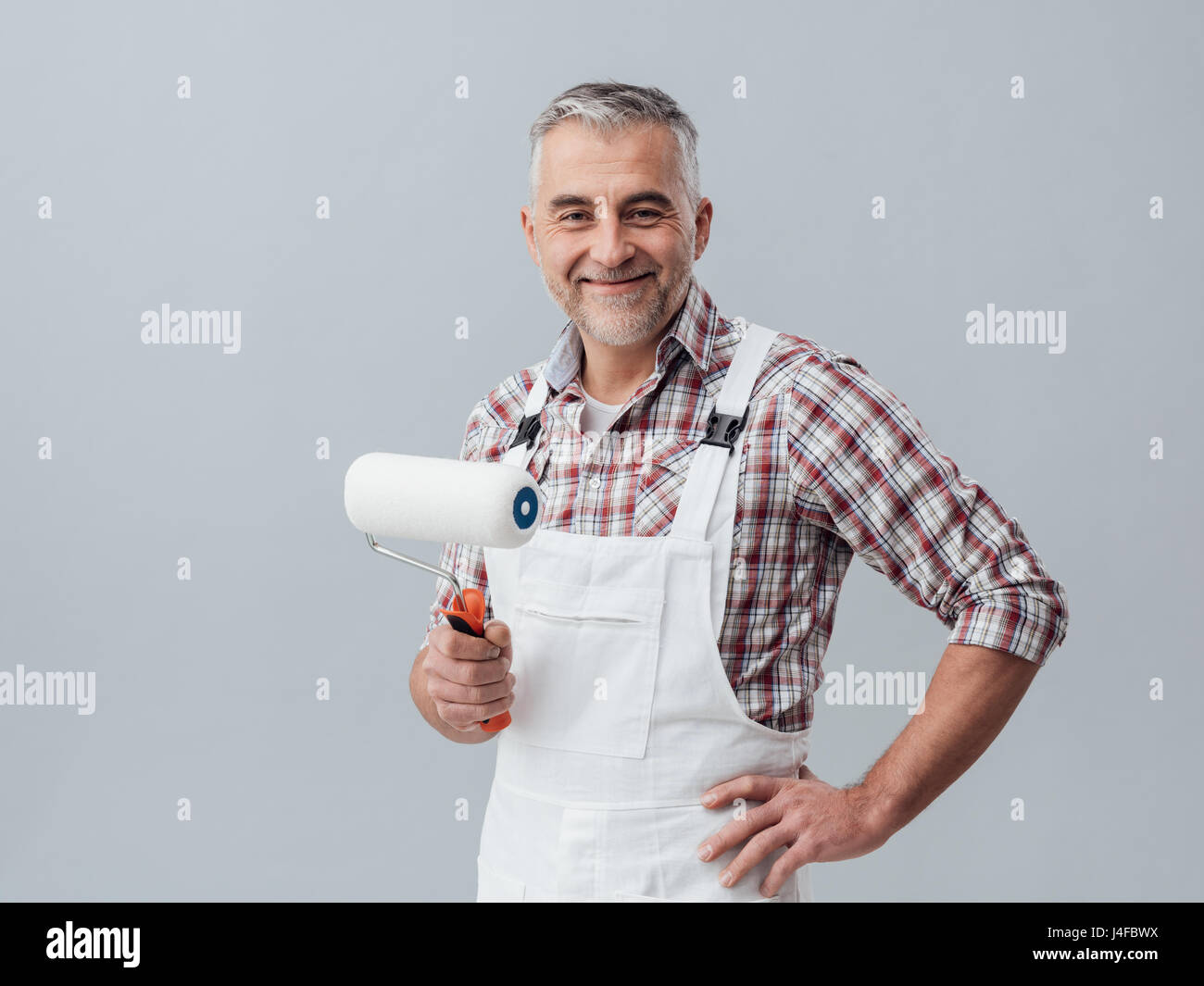 Confident smiling painter and decorator posing with a paint roller ...