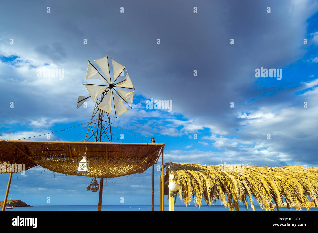 Decorative windmill with white propeller installed on thatched roof ...