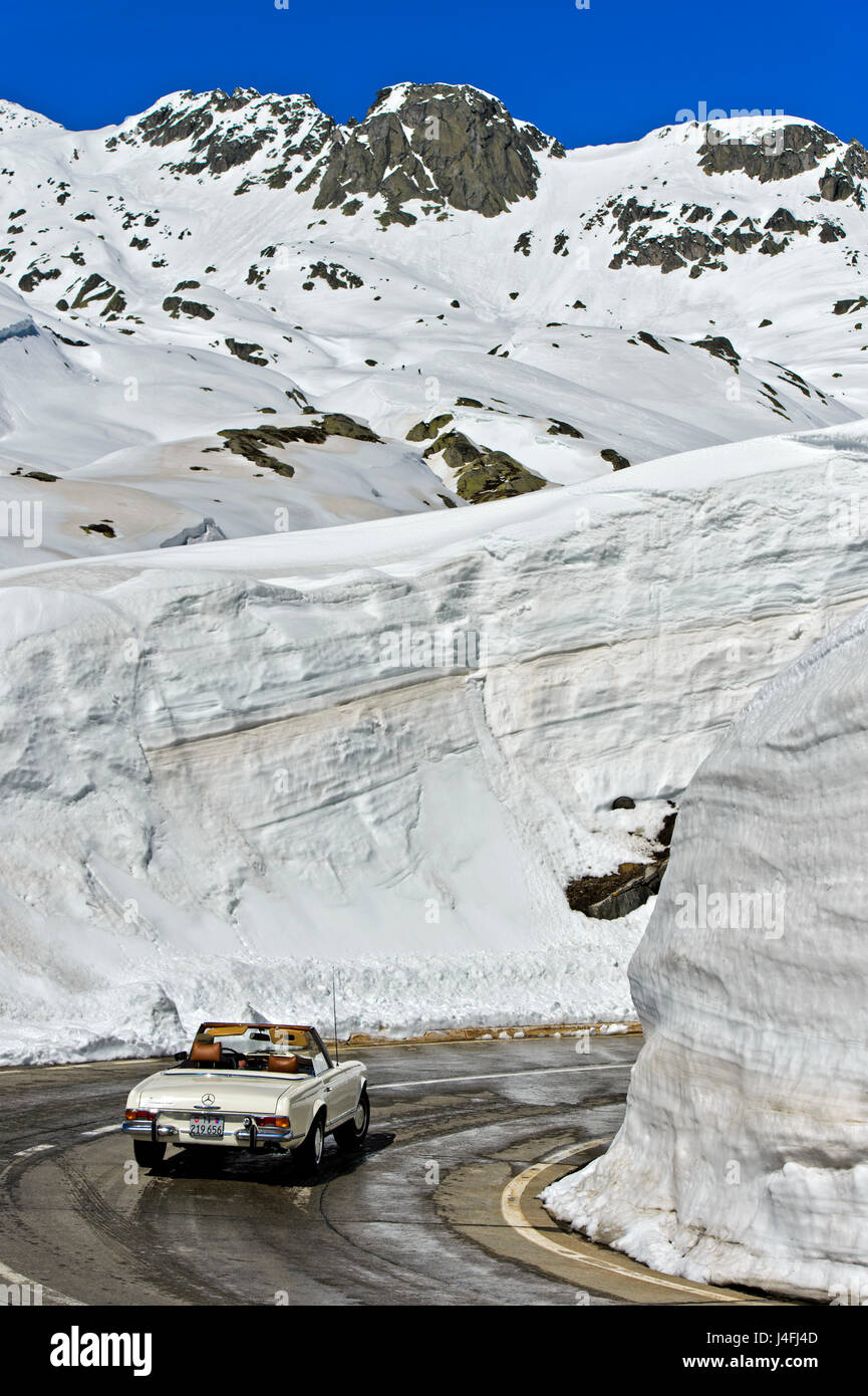Cabriolet driving on the pass road between high snow walls across the ...