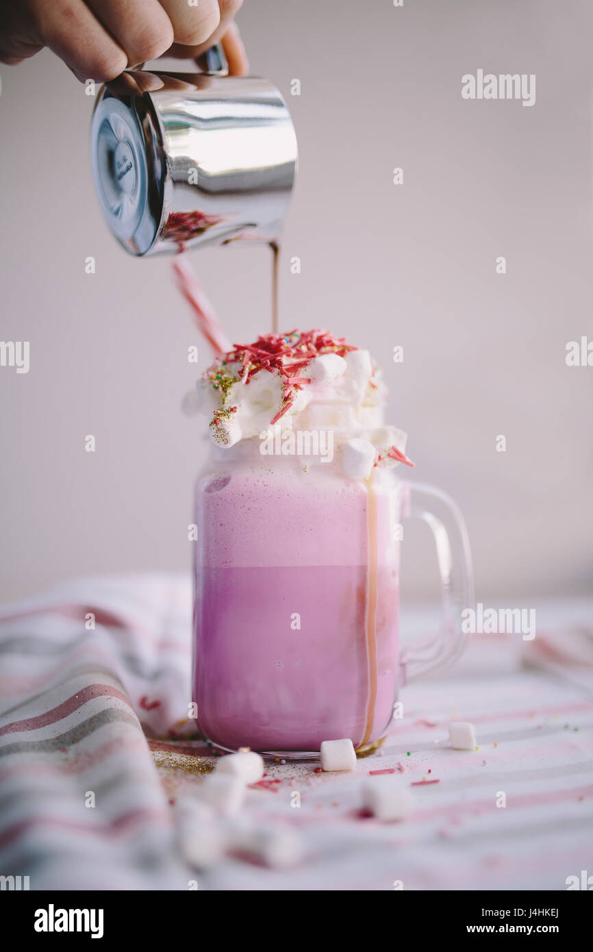 Woman is pouring coffee in stylized mason jar cup of colored milk with ...