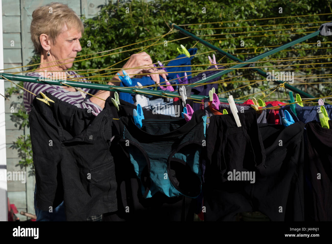 Grandmother hanging out the washing in the sunshine using a rotary line ...