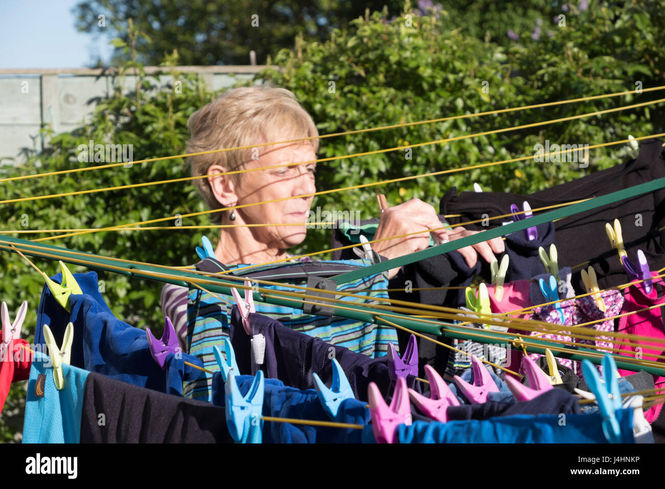 Grandmother hanging out the washing in the sunshine using a rotary line ...