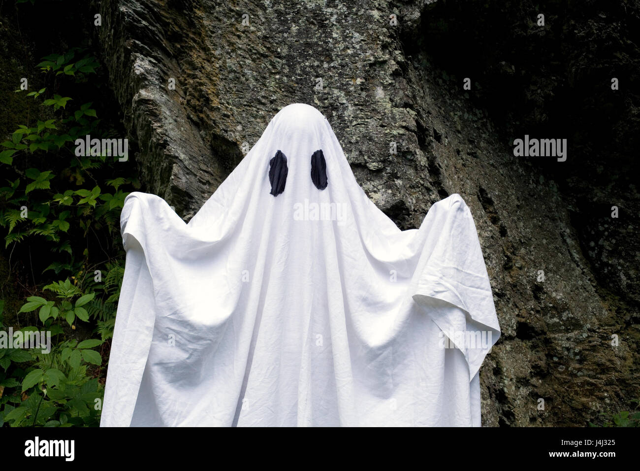 A spooky white ghost covered by a sheet with slits over the eyes ...