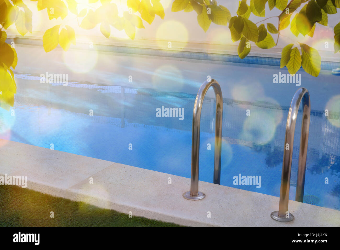 Pool ladder in pool with blue mosaic tiles. With leaves of tree and sun ...