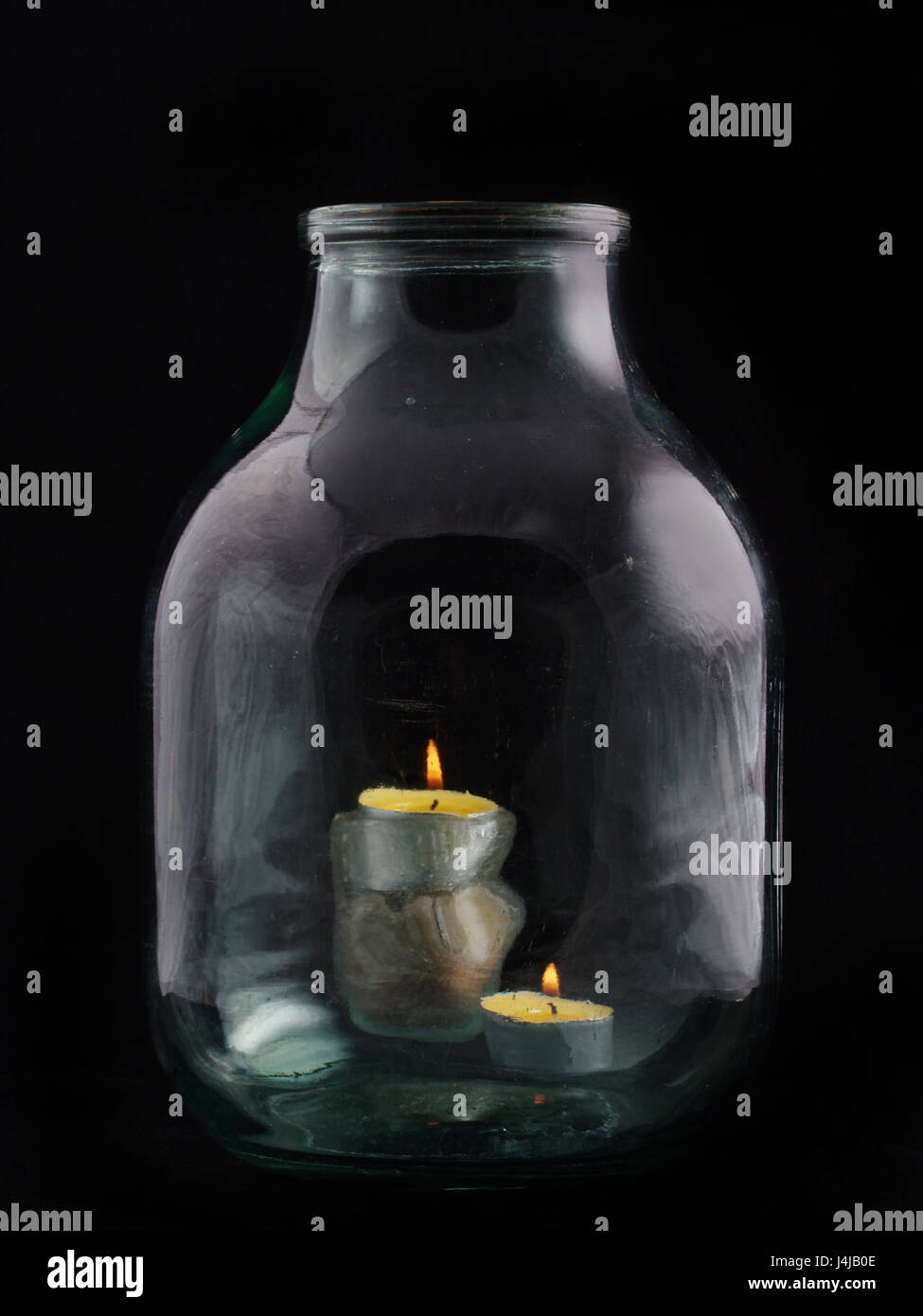 Two burning candles inside a large glass transparent jar on a black ...