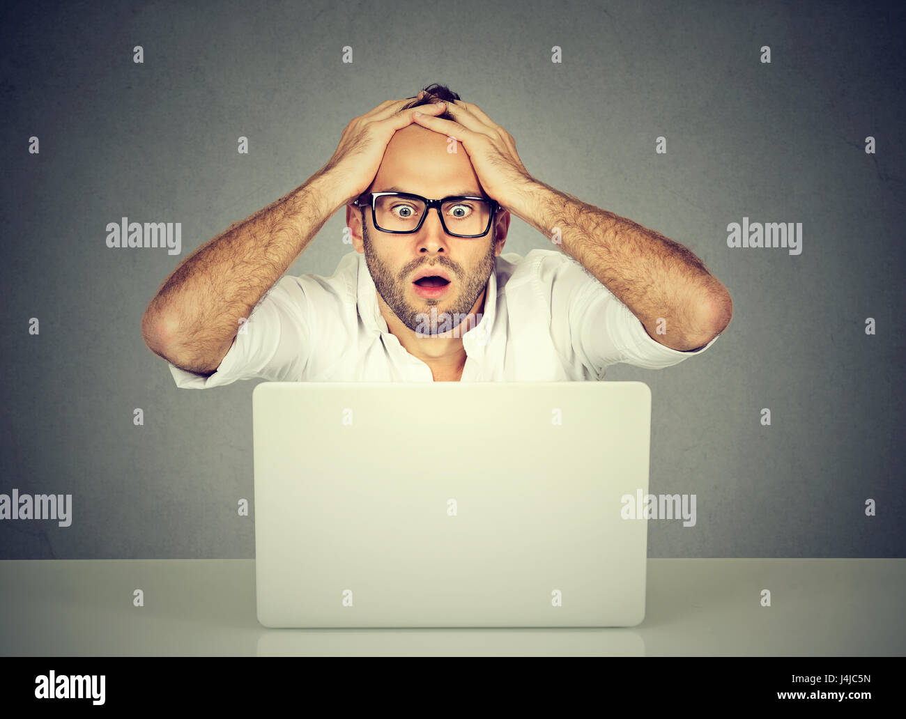 Shocked young man looking at laptop computer anxious with open mouth ...