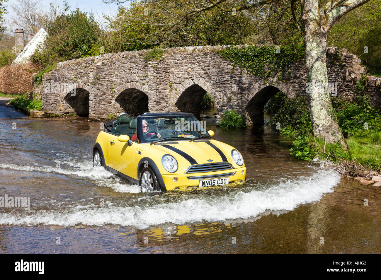 A smiling woman driving a convertible Mini Cooper through the ford ...
