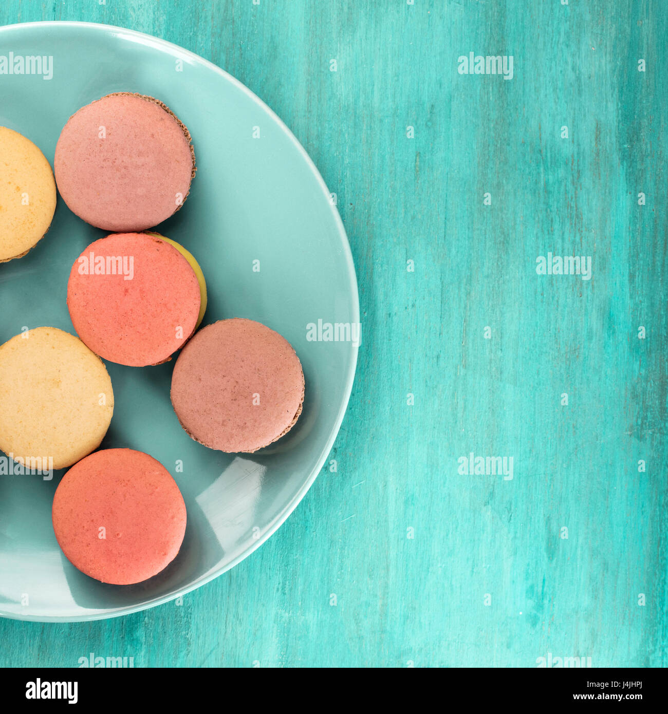 A square photo of macarons on a teal blue plate, shot from above on a ...