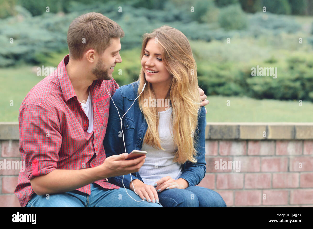 Couple listening to the music with earbuds from a smart phone in a park ...