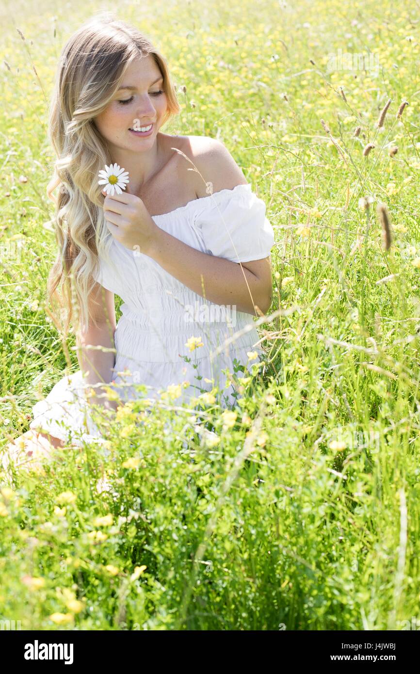 Young woman sitting in meadow holding daisy Stock Photo - Alamy