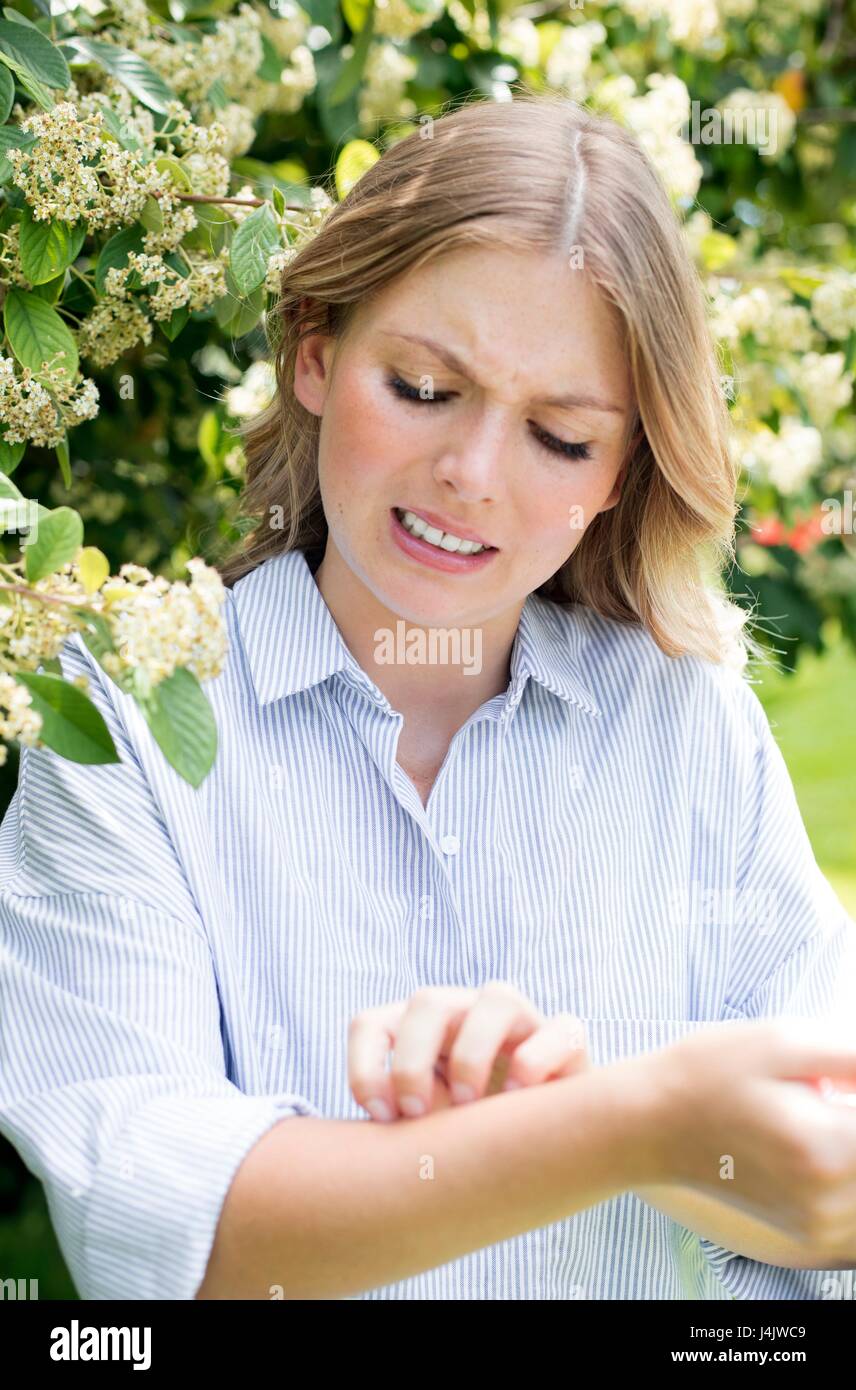 Young woman by tree scratching arm Stock Photo - Alamy