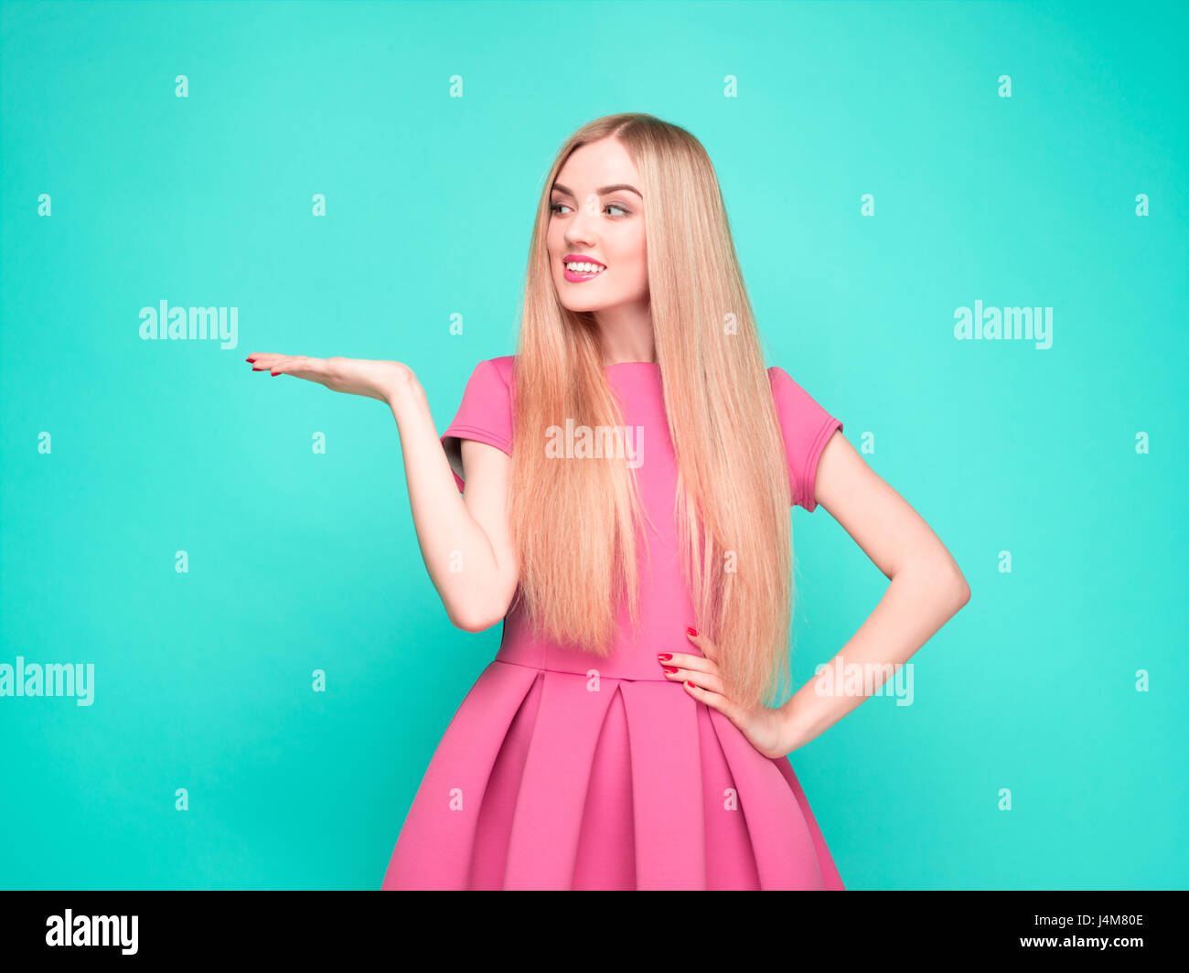 Smiling beautiful young woman in pink mini dress posing, presenting ...
