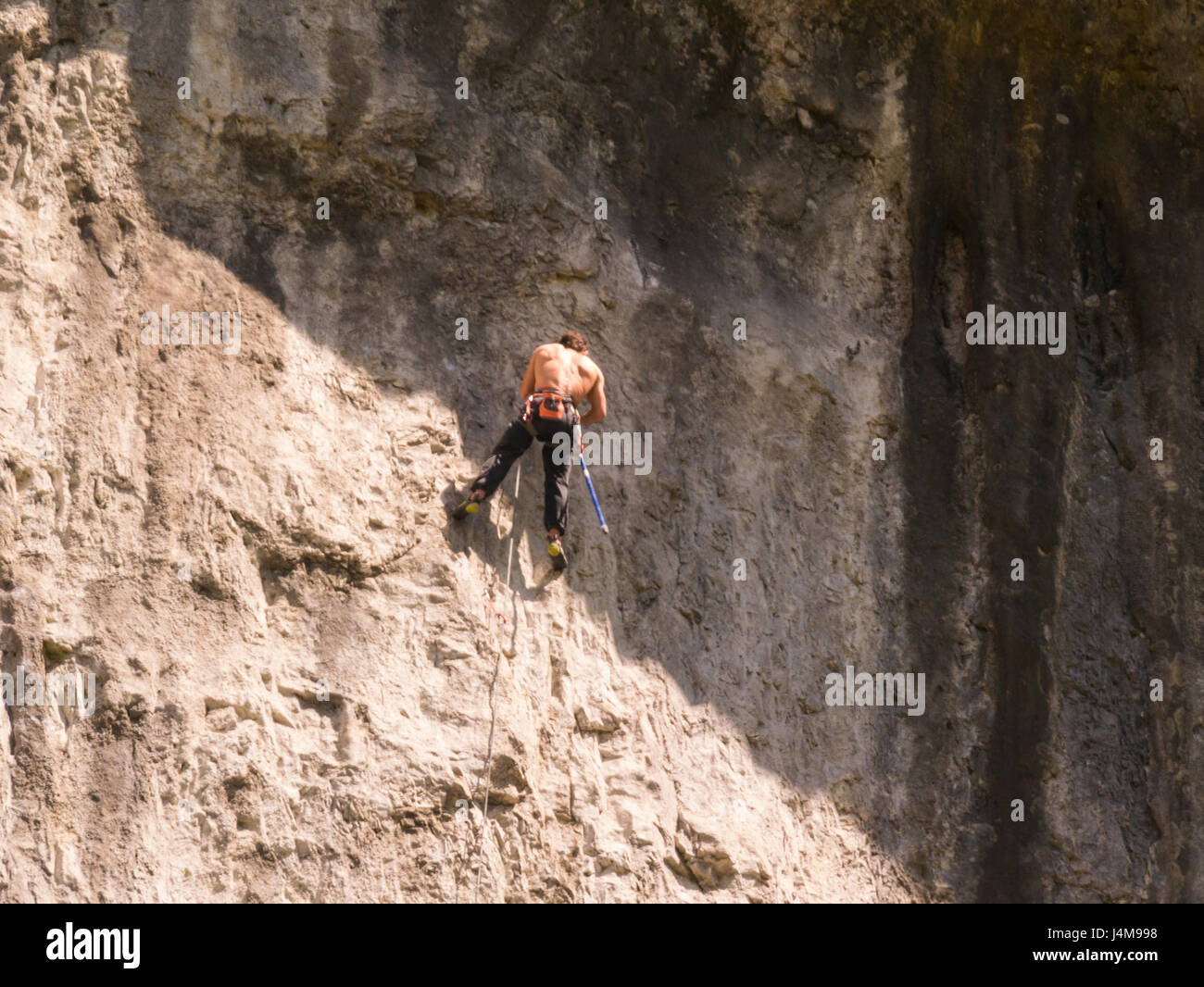 Young bare chested man climbing the limestone escarpment of Malham Cove ...