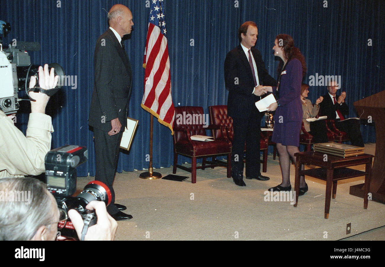 A MAN AND WOMEN AT THE PODIUM SHACKING HANDS WITH OTHER PEOPLE WATCHING ...