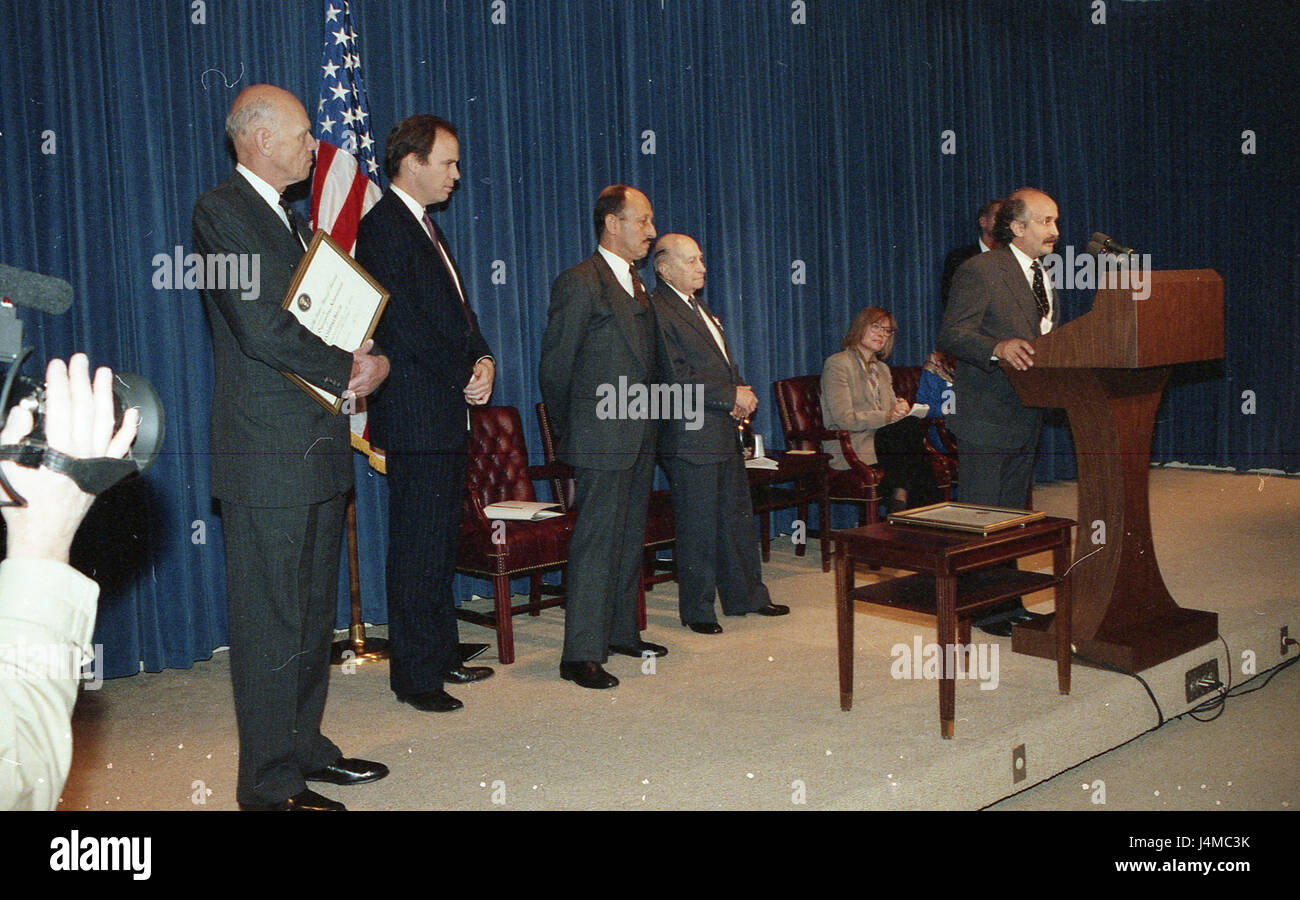 A MAN AT THE PODIUM GIVING A SPEECH WITH OTHER PEOPLE WATCHING Stock ...