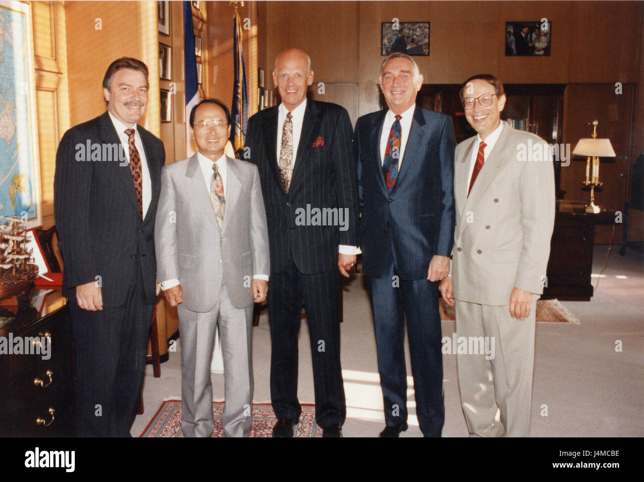Five men stand together in an office setting for a group photograph ...