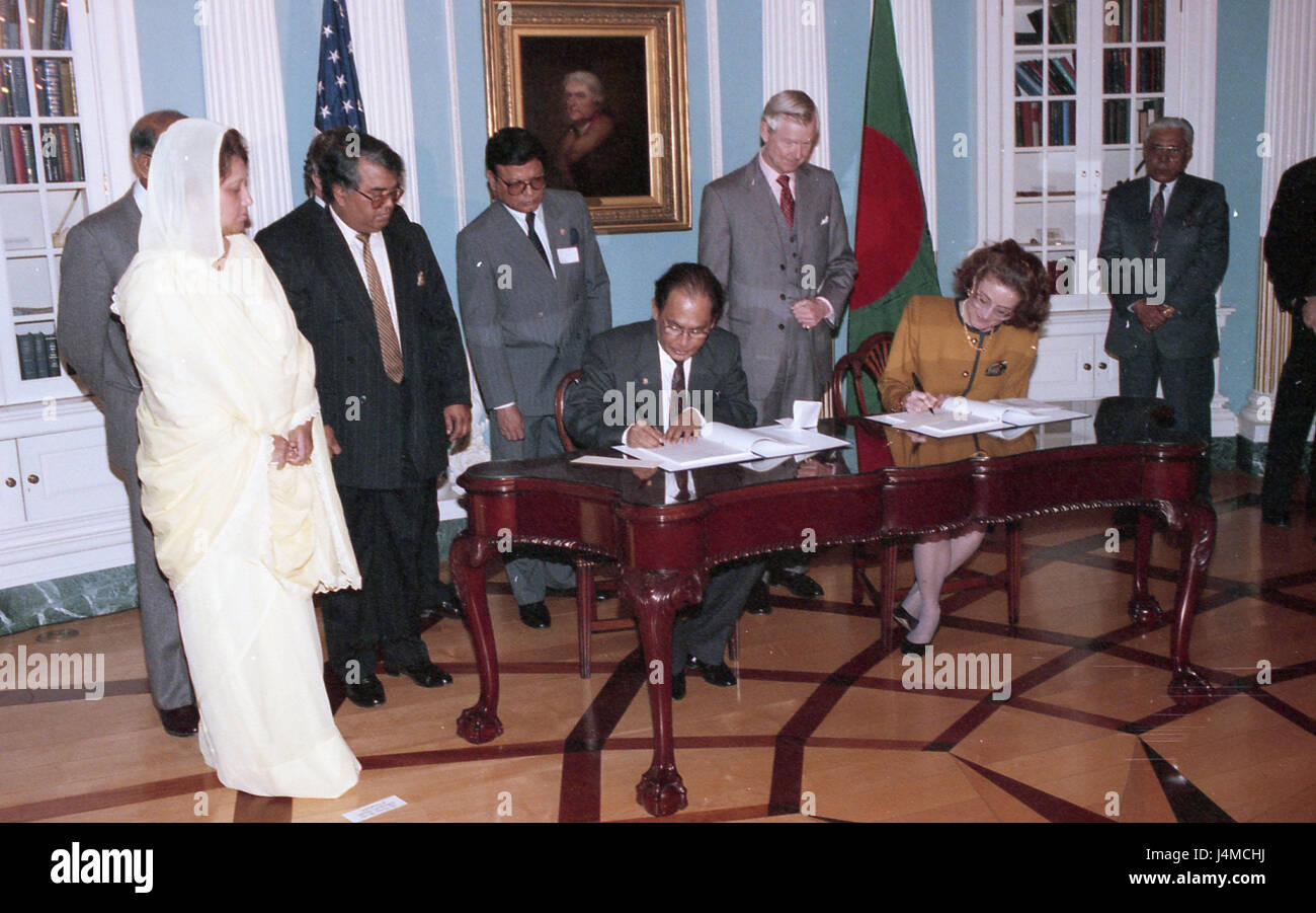 A group of individuals observes the signing of official documents ...