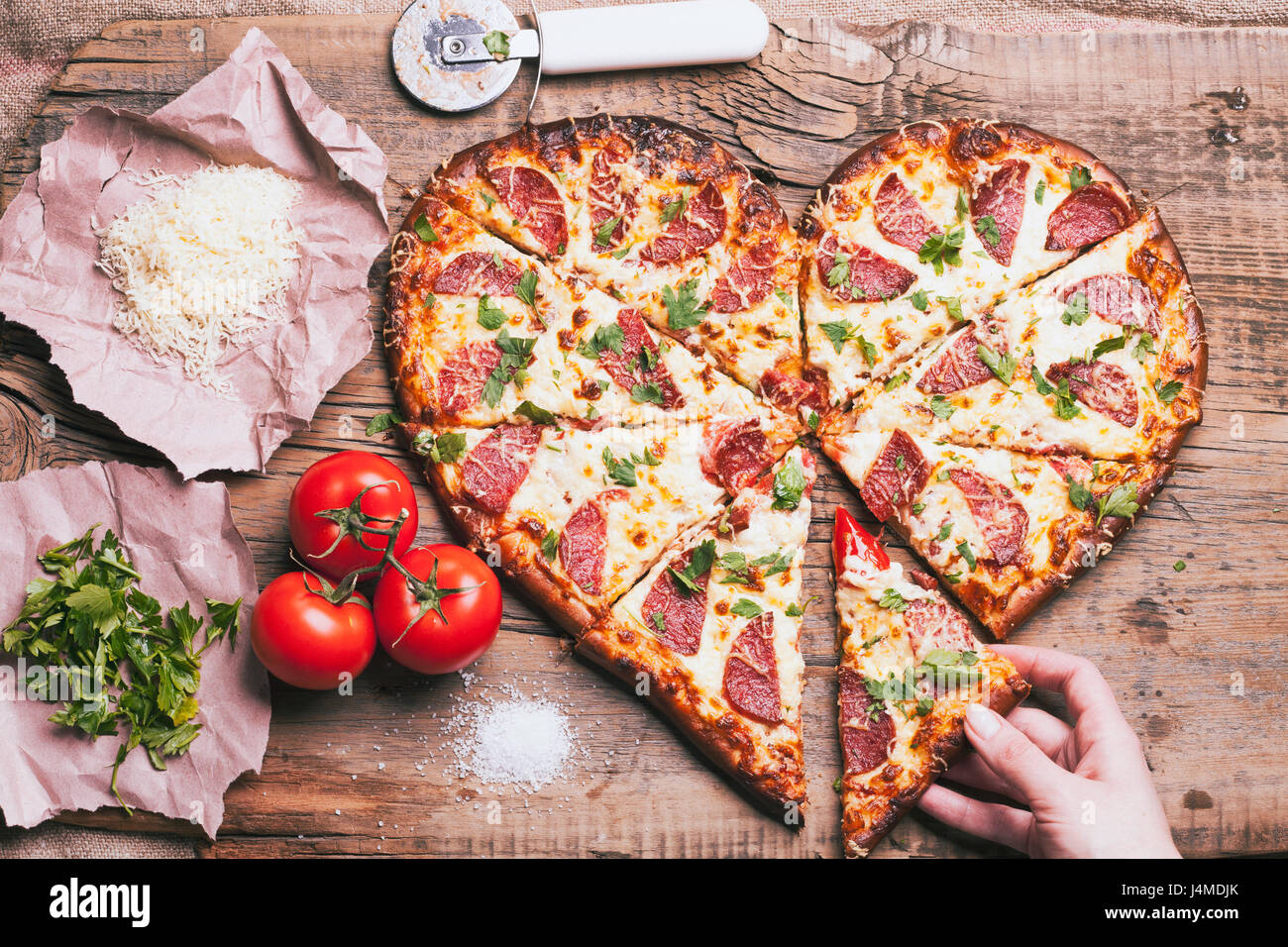 Hand pulling slice of heart-shaped pizza near ingredients on cutting ...