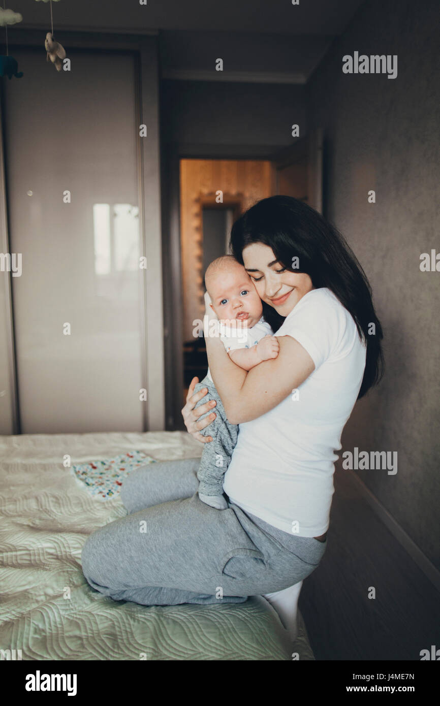 Caucasian mother kneeling on bed hugging baby son Stock Photo - Alamy