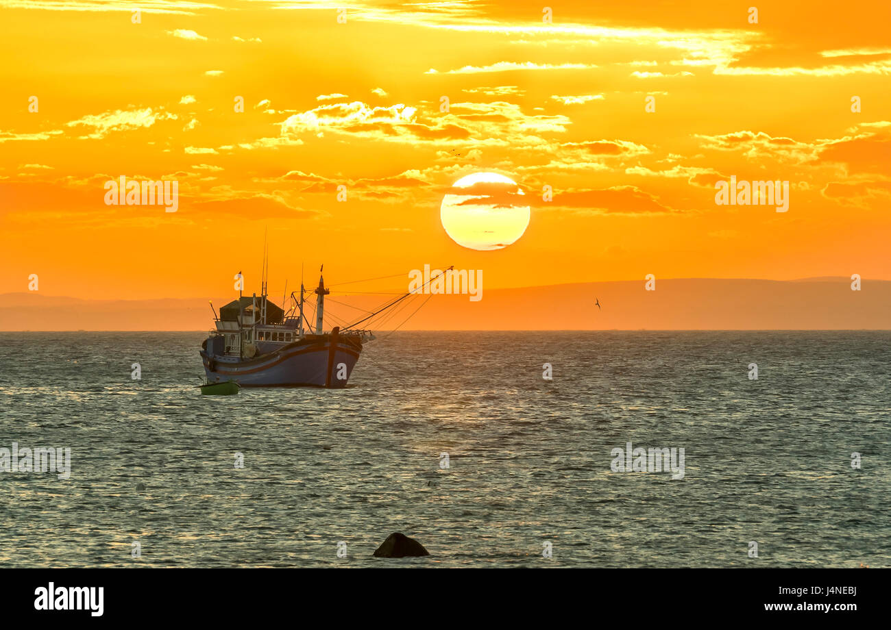 Sunset and boat on the sea as the sun slowly down the horizon circle ...