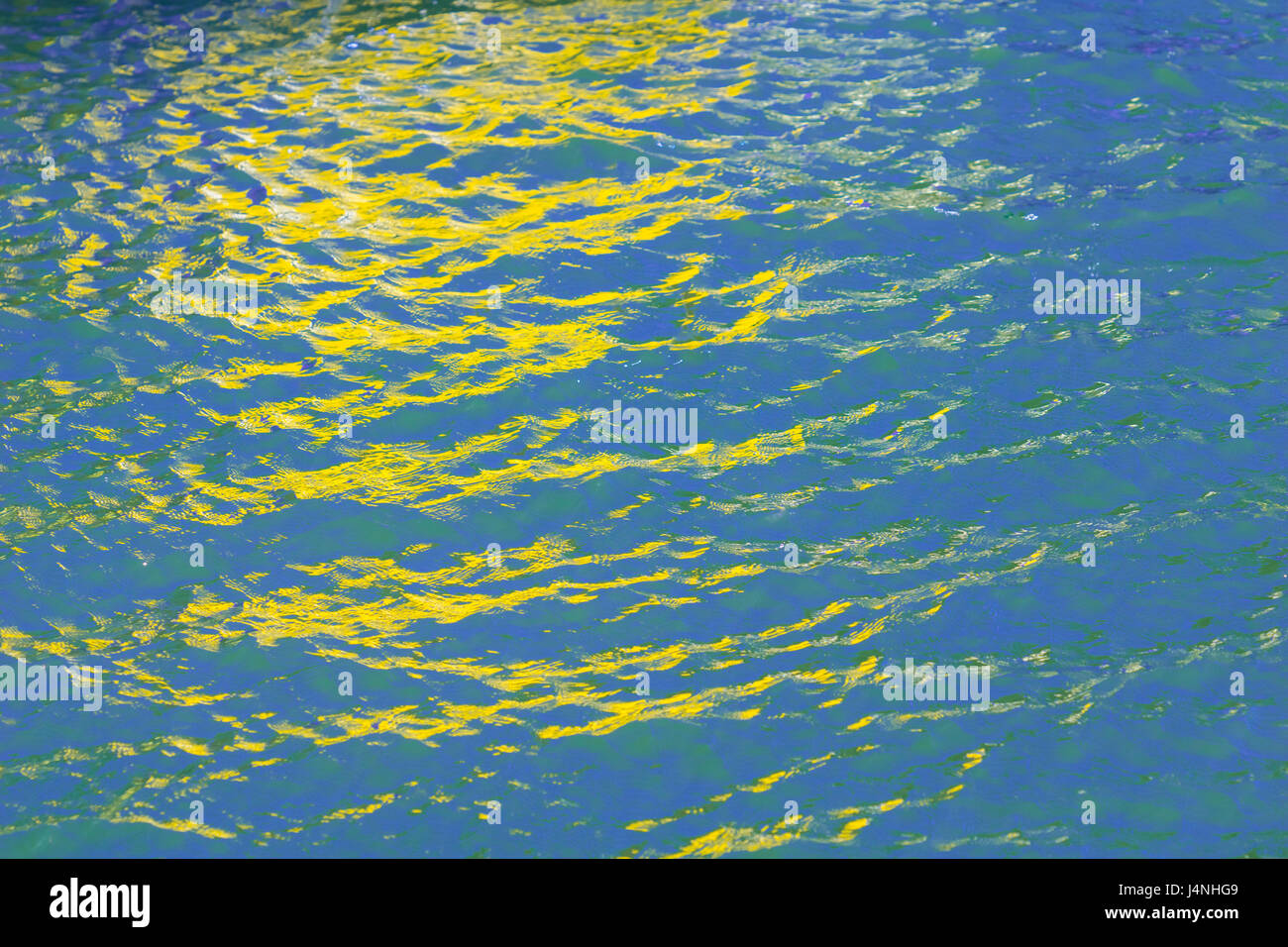 Yellow on blue water shimmering reflected colors of yellow and green on ...