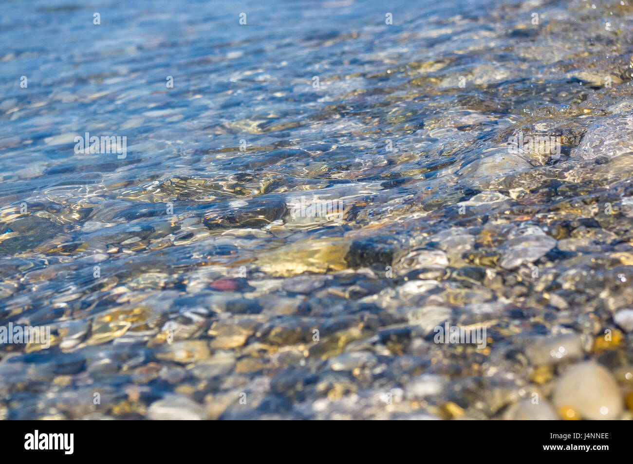 sea pebble beach with multicoloured stones, transparent waves with foam ...