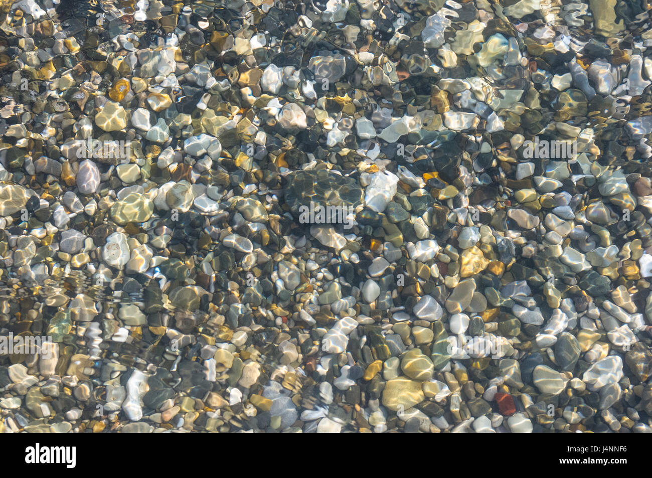 sea pebble beach with multicoloured stones, transparent waves with foam ...