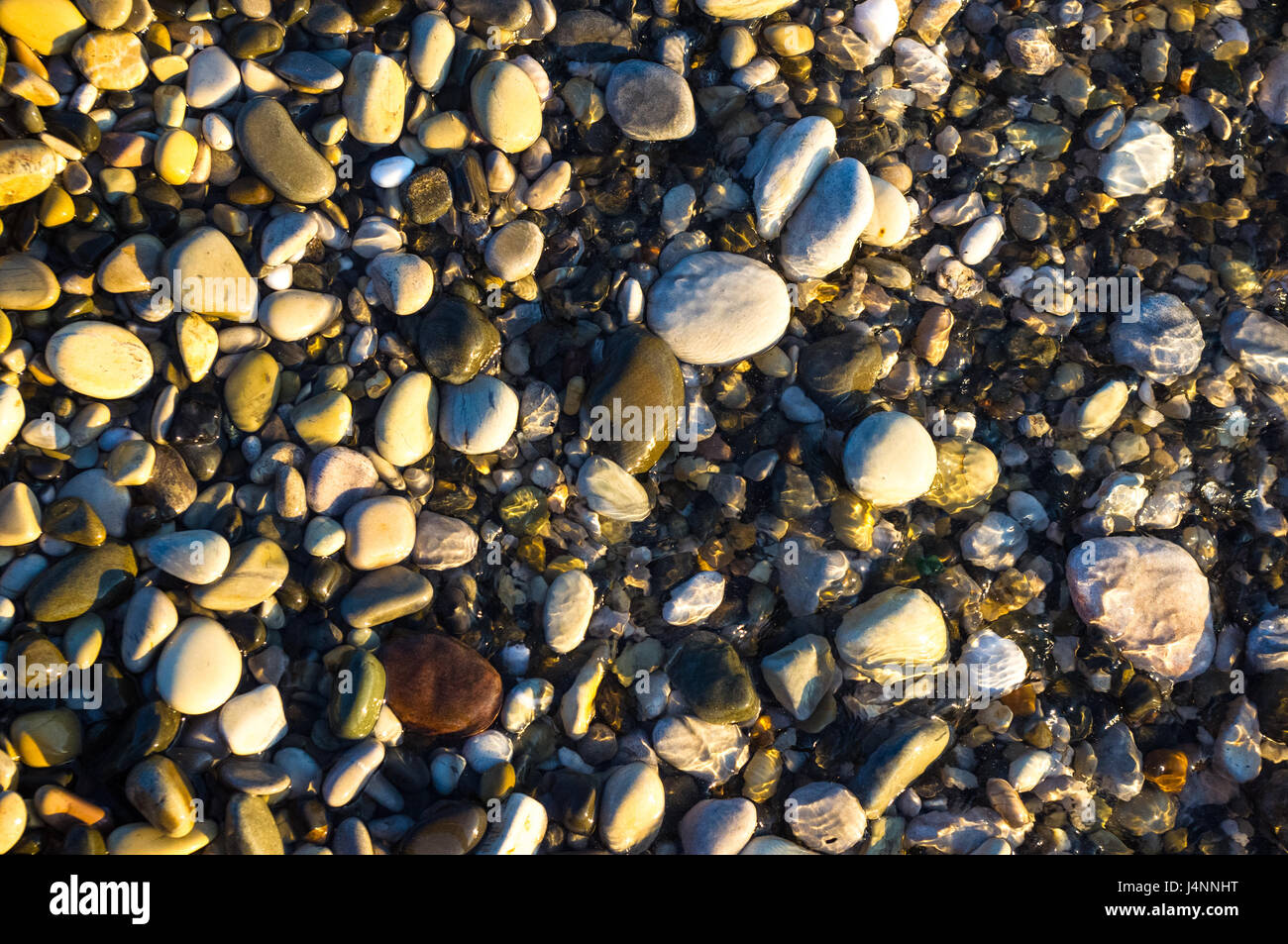 sea pebble beach with multicoloured stones, transparent waves with foam ...