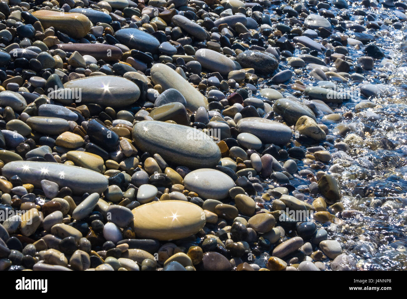 sea pebble beach with multicoloured stones, transparent waves with foam ...