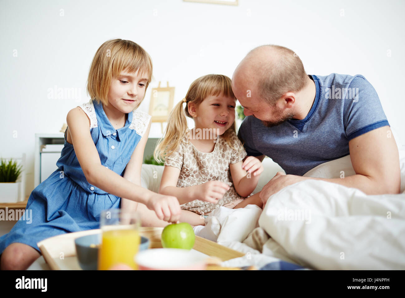 Little girl talking to father in the morning with her sister near by ...