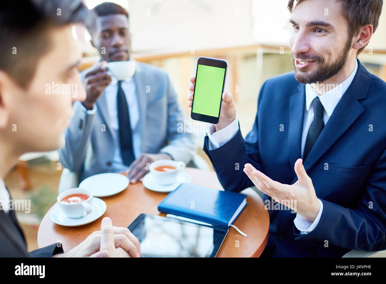 Portrait of modern young businessman enthusiastically presenting mobile ...