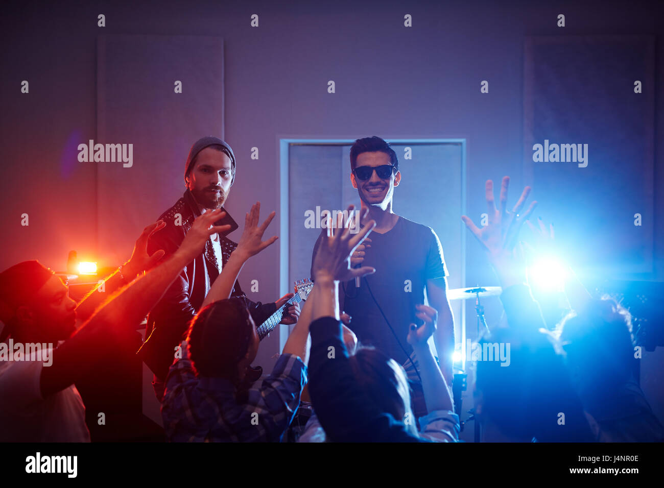 Handsome musicians performing on stage of urban club with crowd of ...