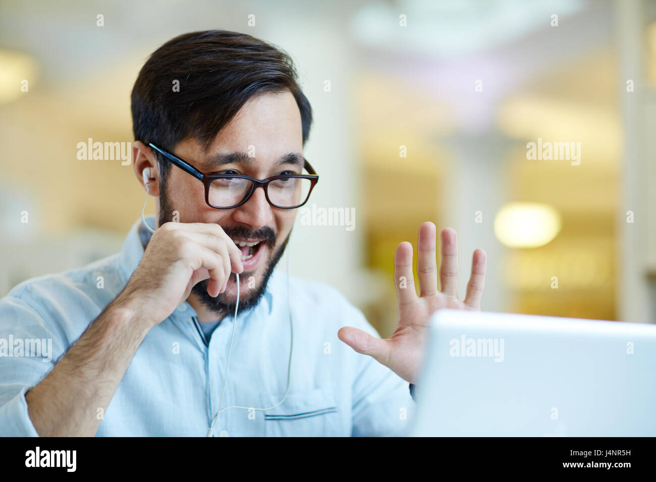 Young man saying hello and waving hand while talking through video-chat ...