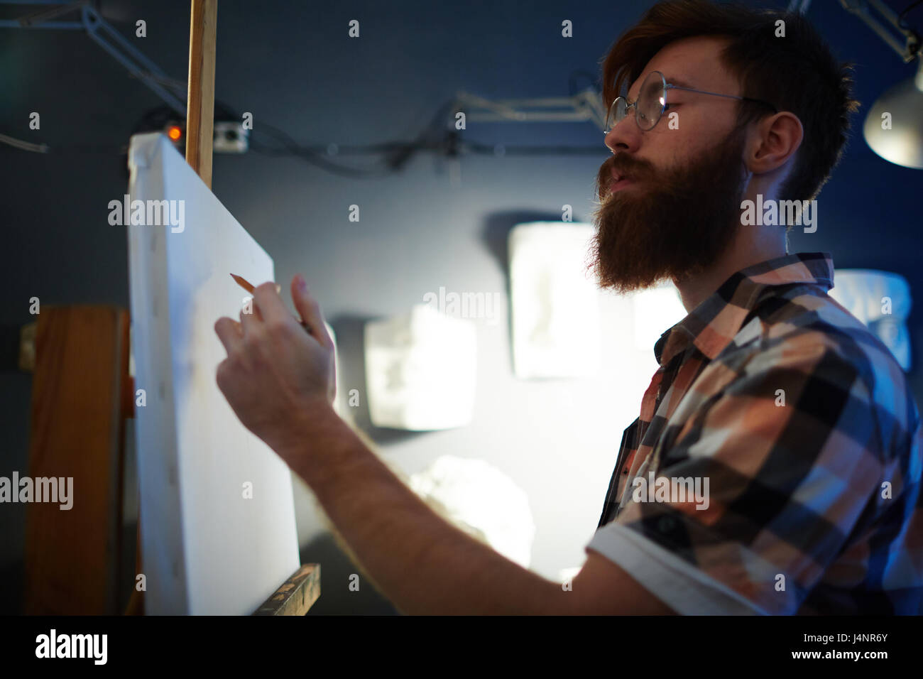 Portrait of inspired young red-haired man drawing outline on canvas ...