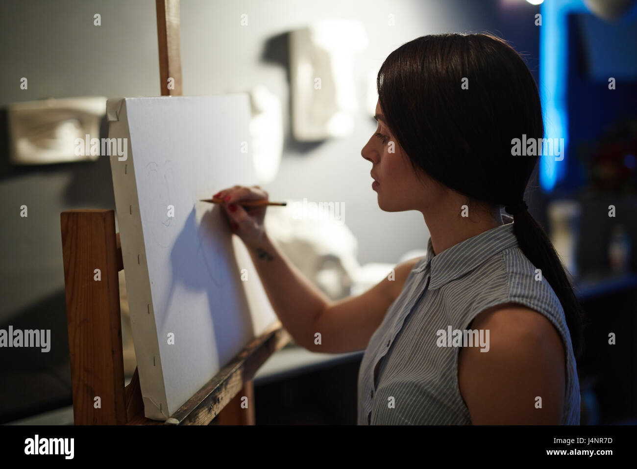 Portrait of talented young woman drawing plaster head models on blank ...
