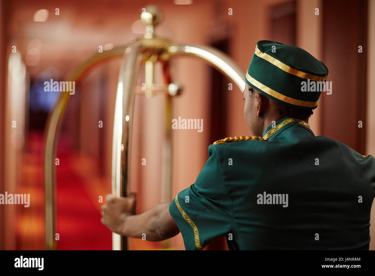 Back view portrait of African-American bellhop pushing luggage cart ...