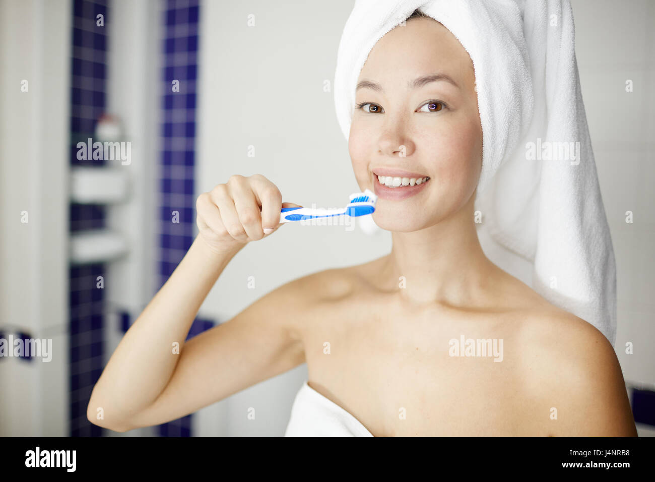 Portrait of smiling Asian woman brushing white teeth in shower during ...