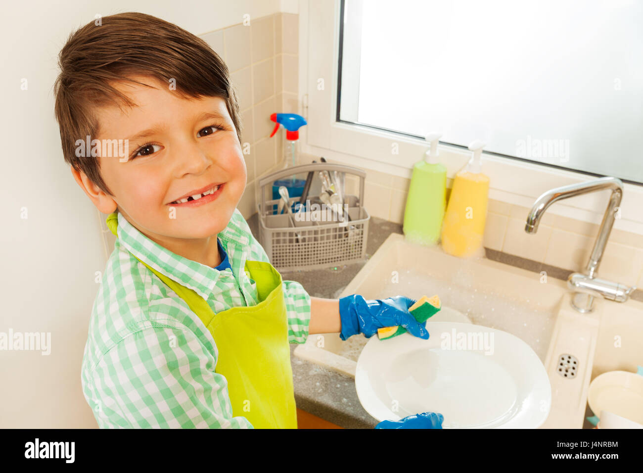Close-up portrait of smiling kid boy washing dishes with sponge ...