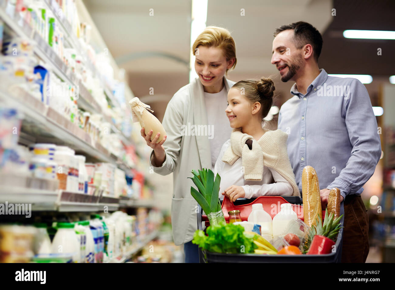 Portrait of happy family shopping in grocery store: choosing milk in ...
