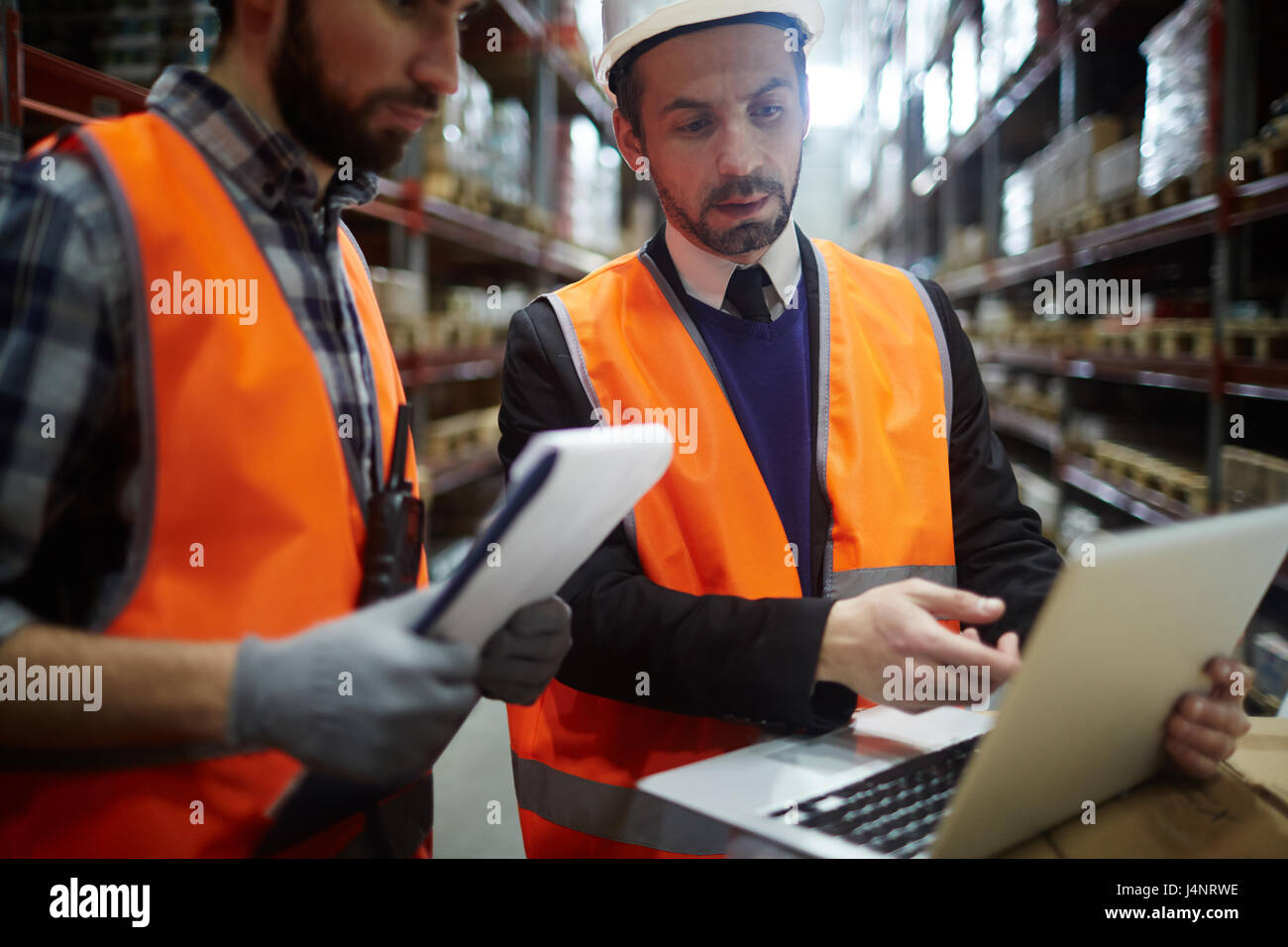 Businessman showing data in laptop to warehouse worker Stock Photo - Alamy
