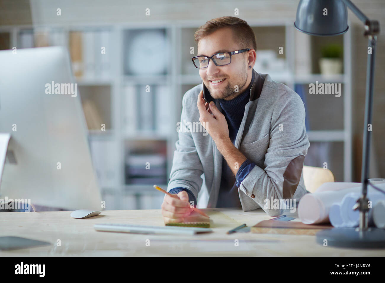 Young man speaking on smartphone while looking at monitor of computer ...