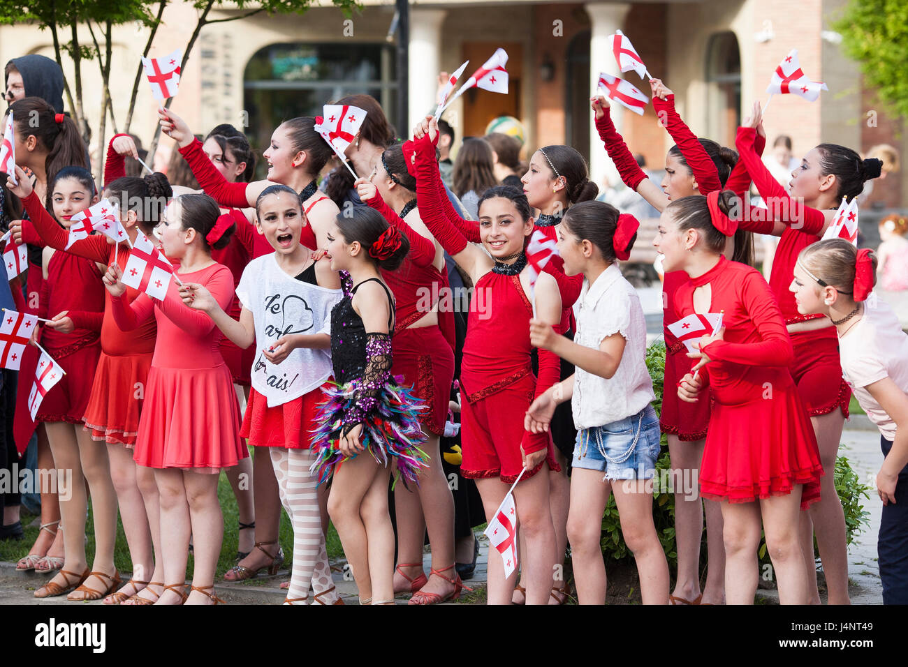 A crowd of children and teens in national costume wave flags to ...