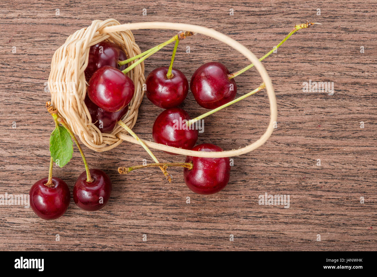 top view of red ripe cherry berries scattered from basket to wooden ...