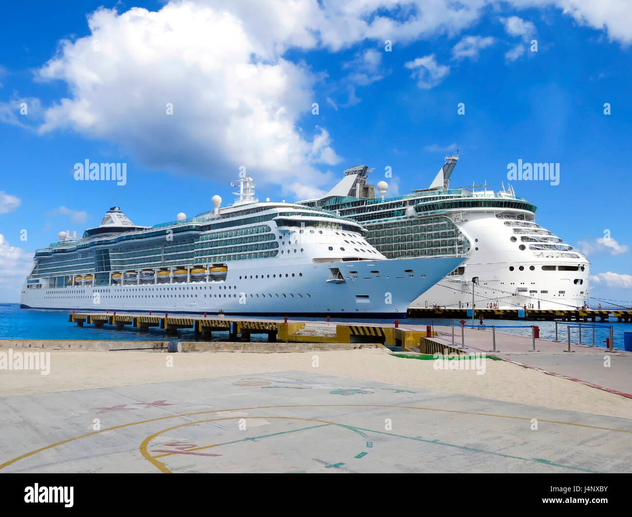 Two Cruise Ships tied together on one pier with blue water and sky ...