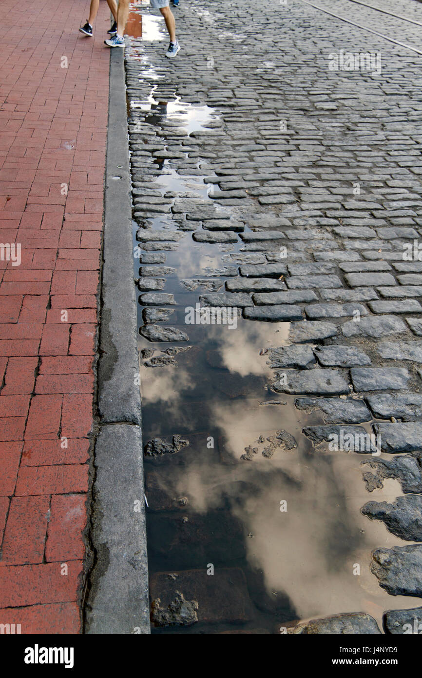 People's legs stepping over long, reflective cobblestone puddles on ...