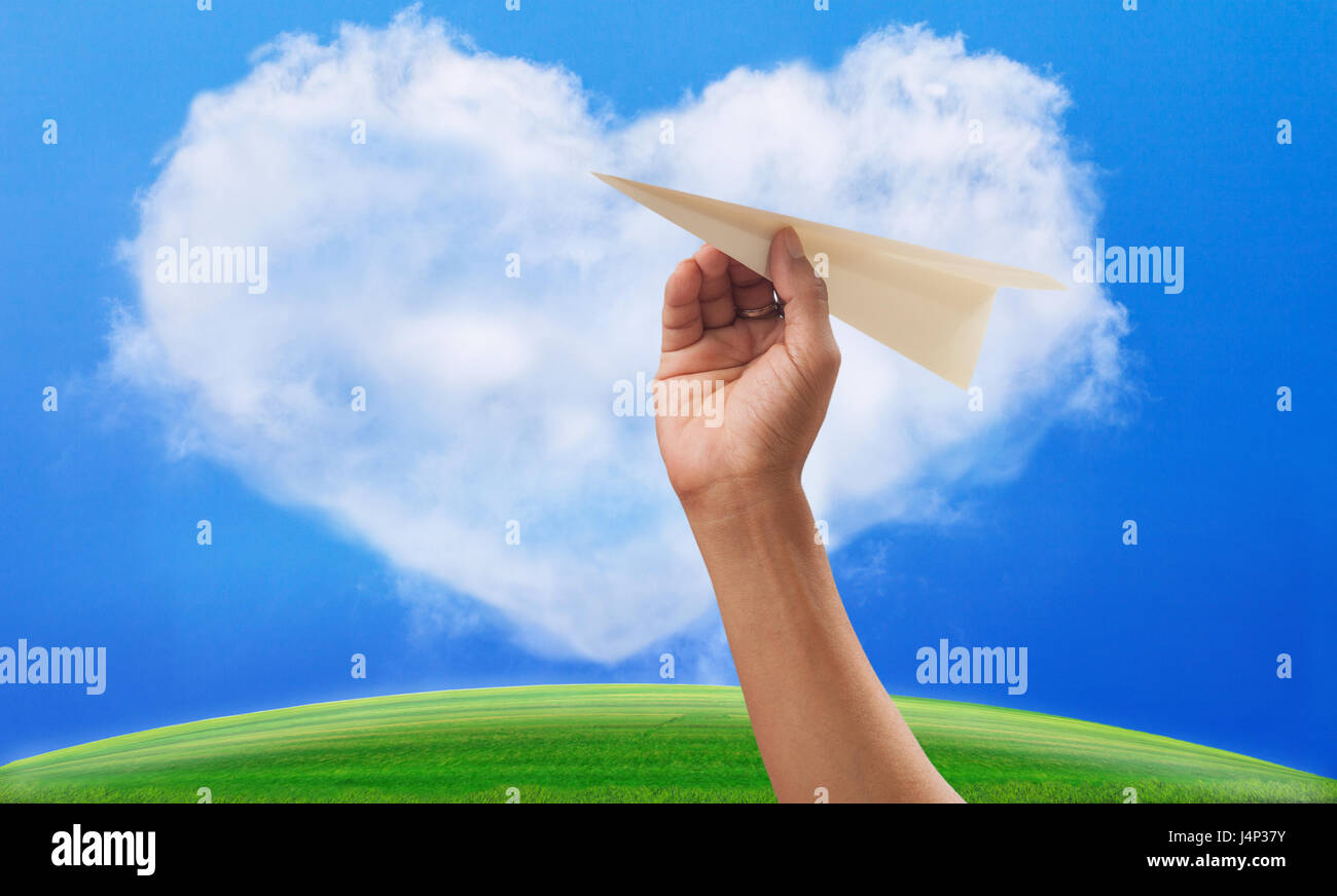 hand preparing to throwing paper plane to mid air againt green grass ...