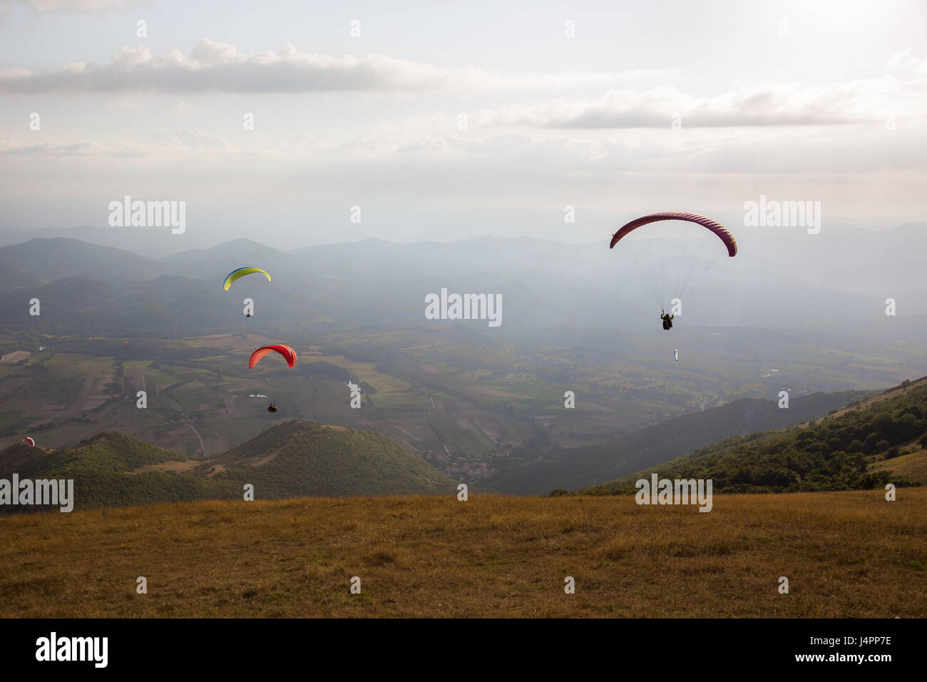 Some colorful paragliders flying over a mountain scenery, with some ...