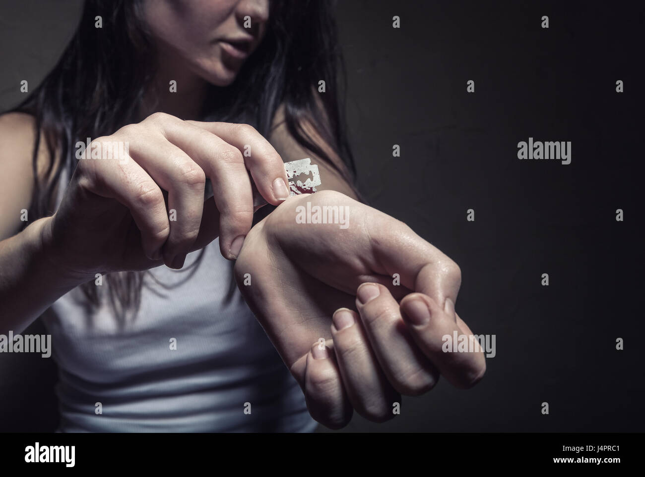 Young woman cuts veins on a hand on a dark background. Focus on hand ...