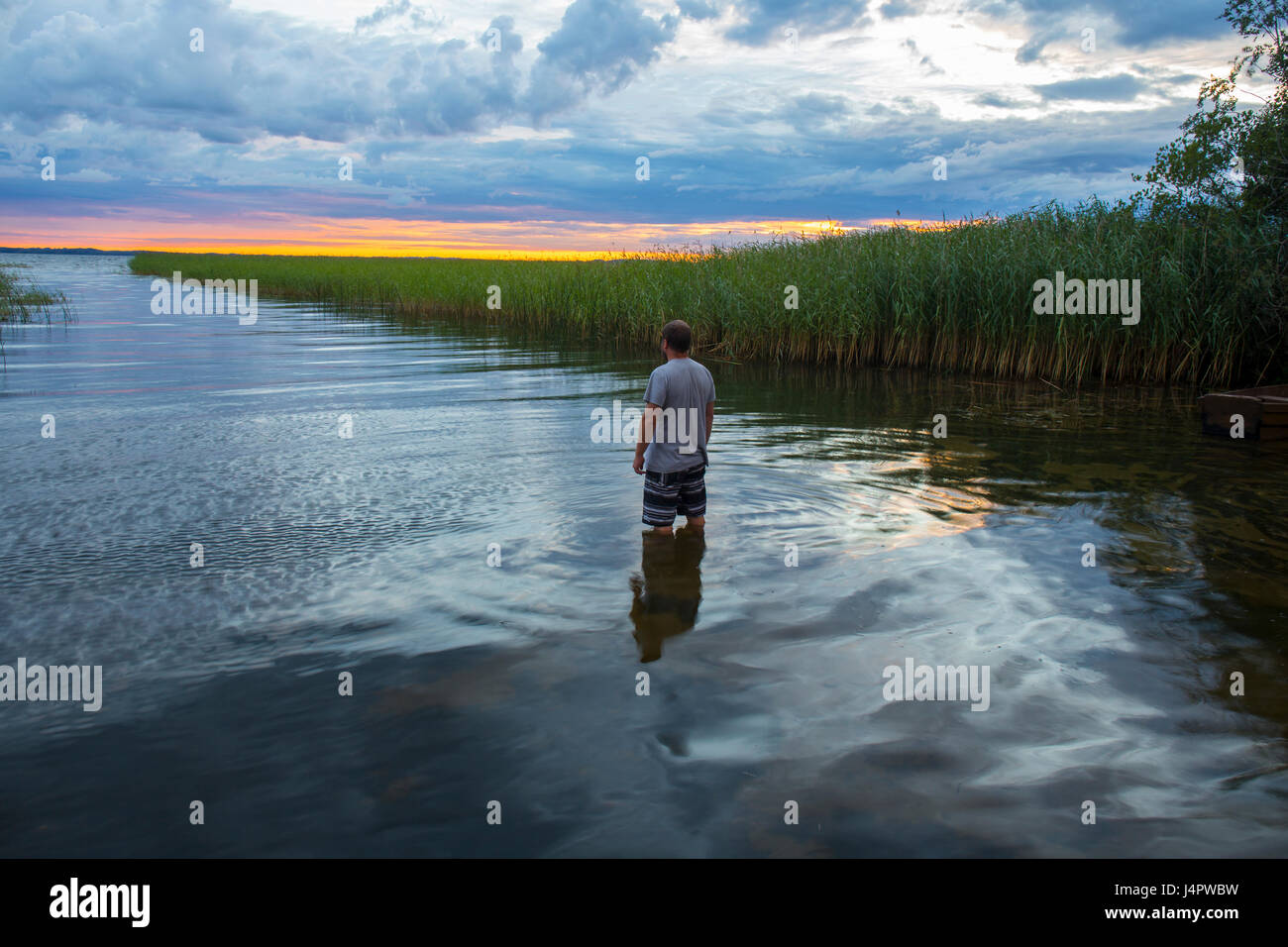 Man standing in a water looking at sunset Stock Photo - Alamy