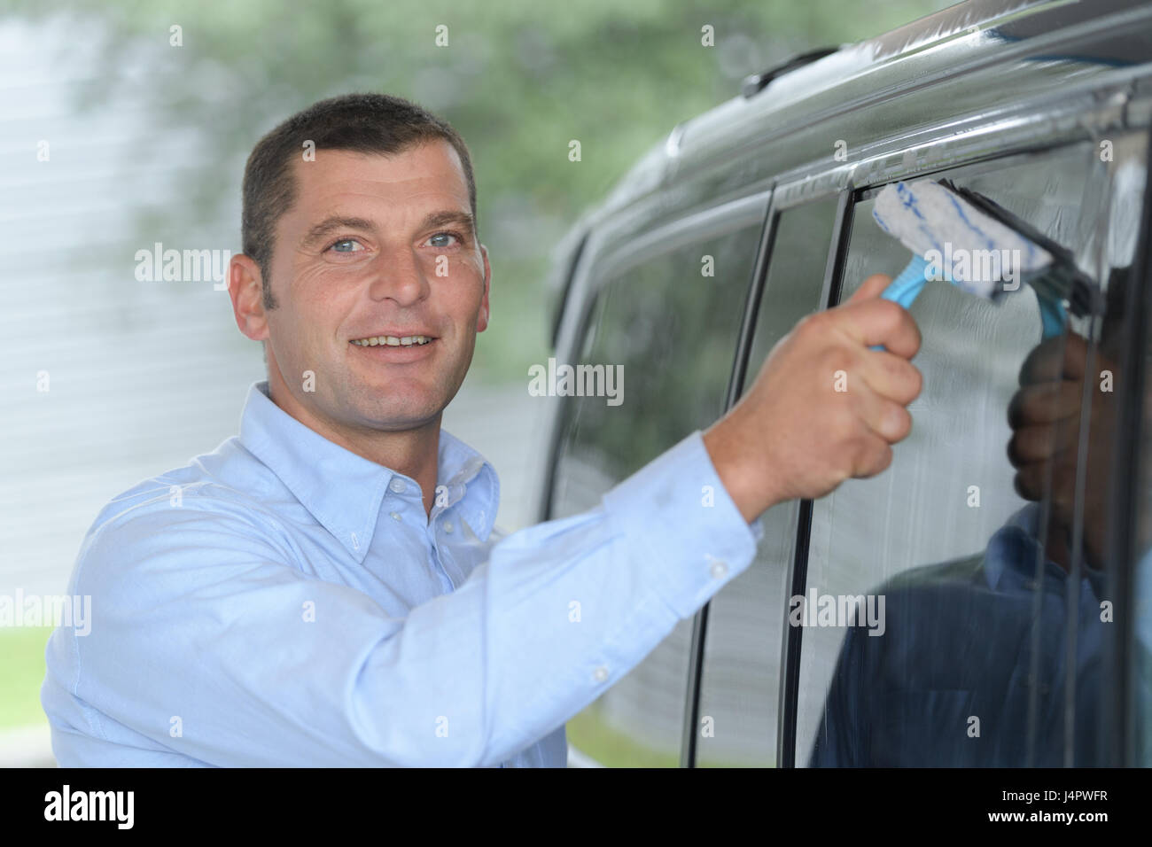 Man cleaning car windows with squeegee Stock Photo - Alamy